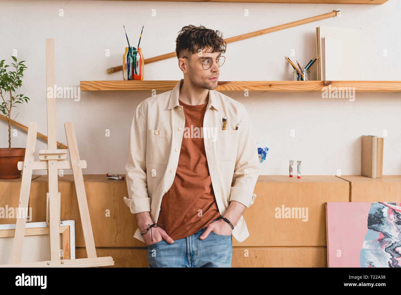 good-looking artist in eyeglasses standing in gallery with hands in ...