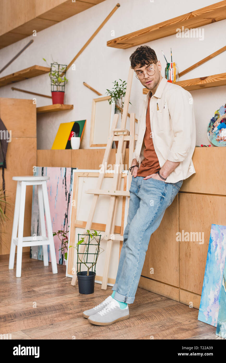 good-looking artist in pink shirt and blue jeans standing in painting ...