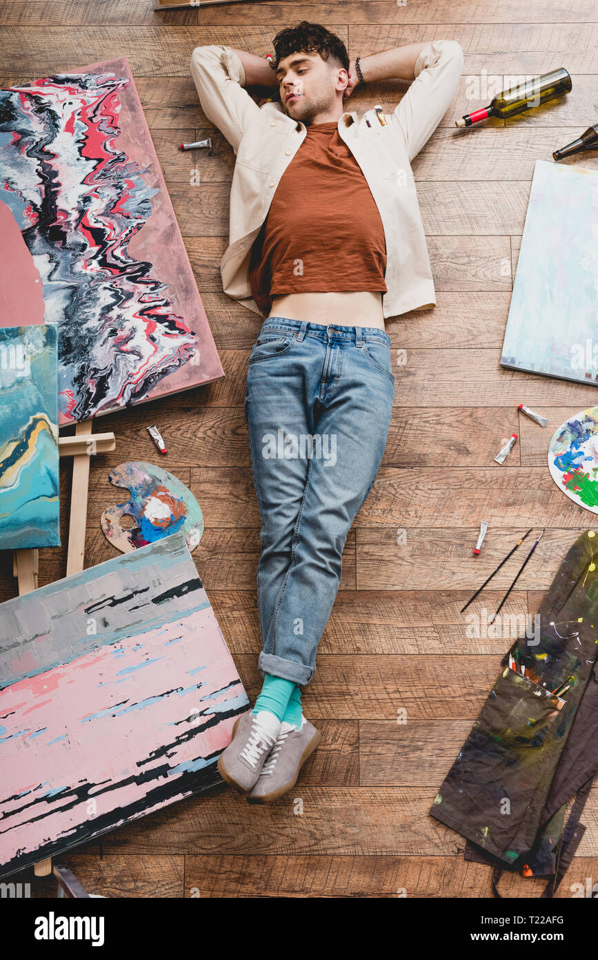 overhead view of tired artist sleeping on floor in painting studio ...