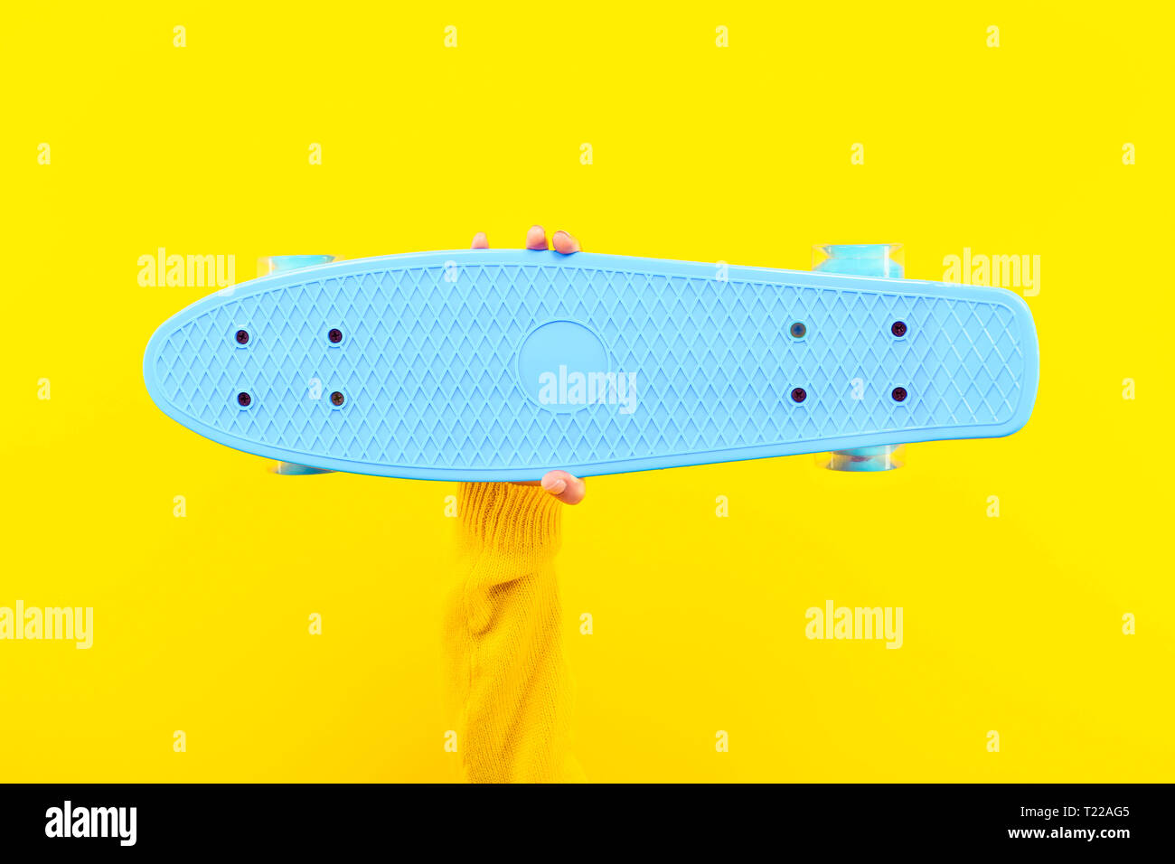 light blue skateboard in hand on yellow background, concept trend and ...
