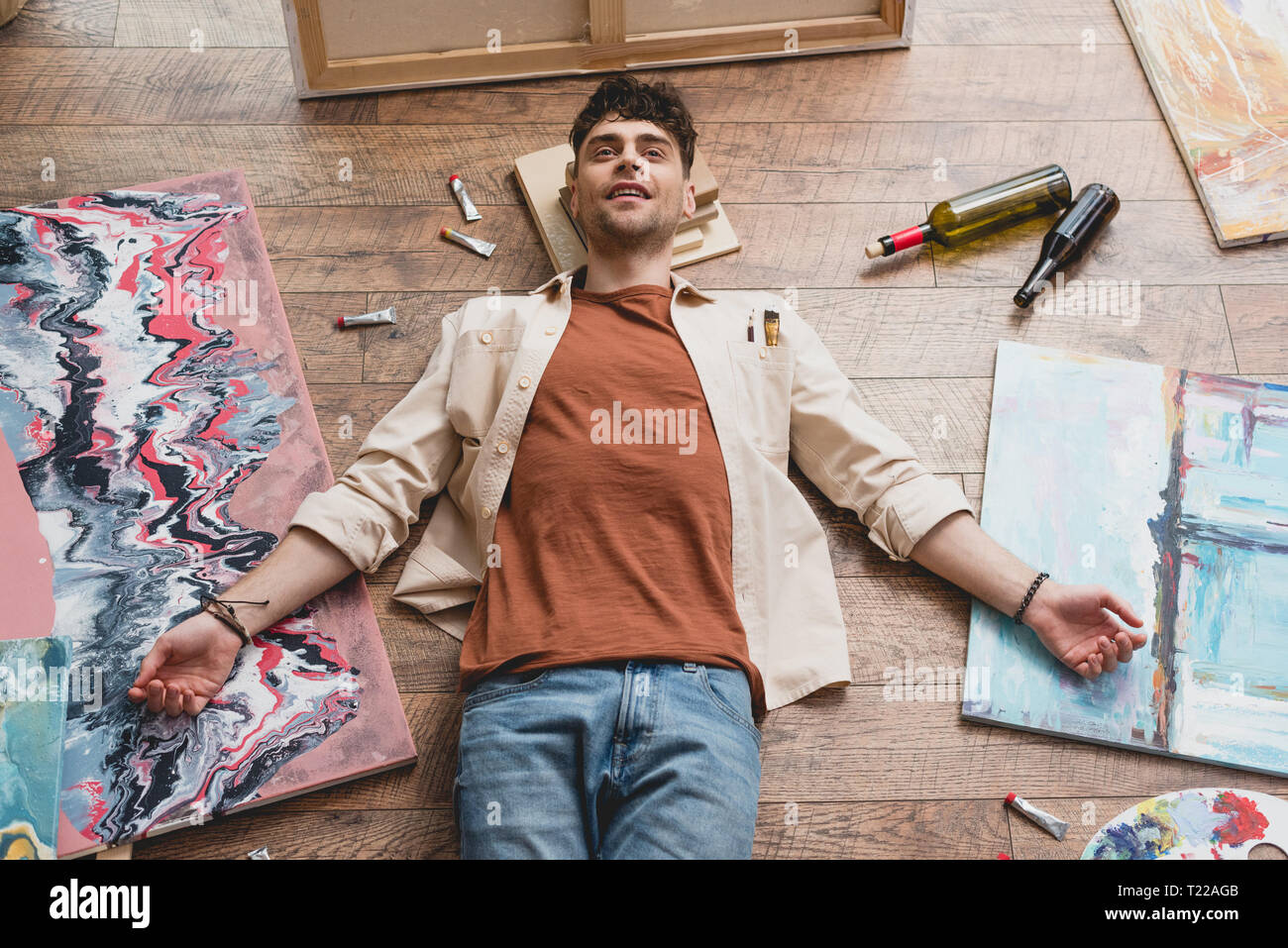 exhausted artist lying on floor in painting studio, surrounded by ...