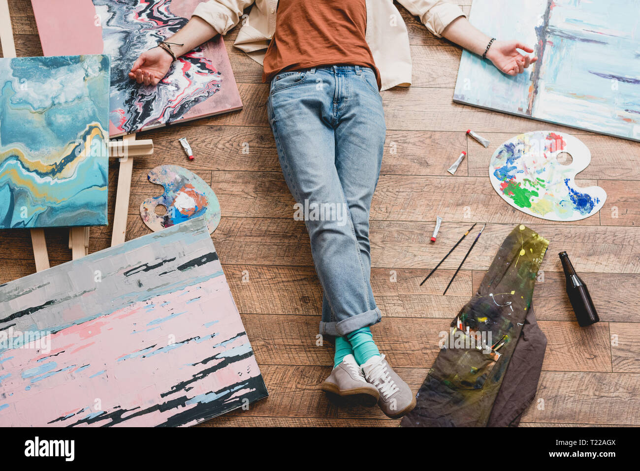 partial view of artist lying of floor, surrounded with painting and ...