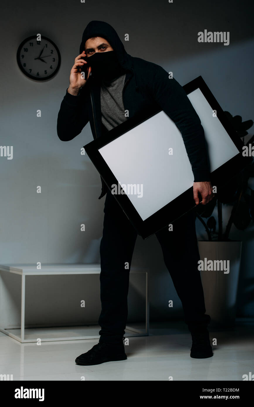 Robber in mask talking on smartphone while stealing flat-screen tv with ...
