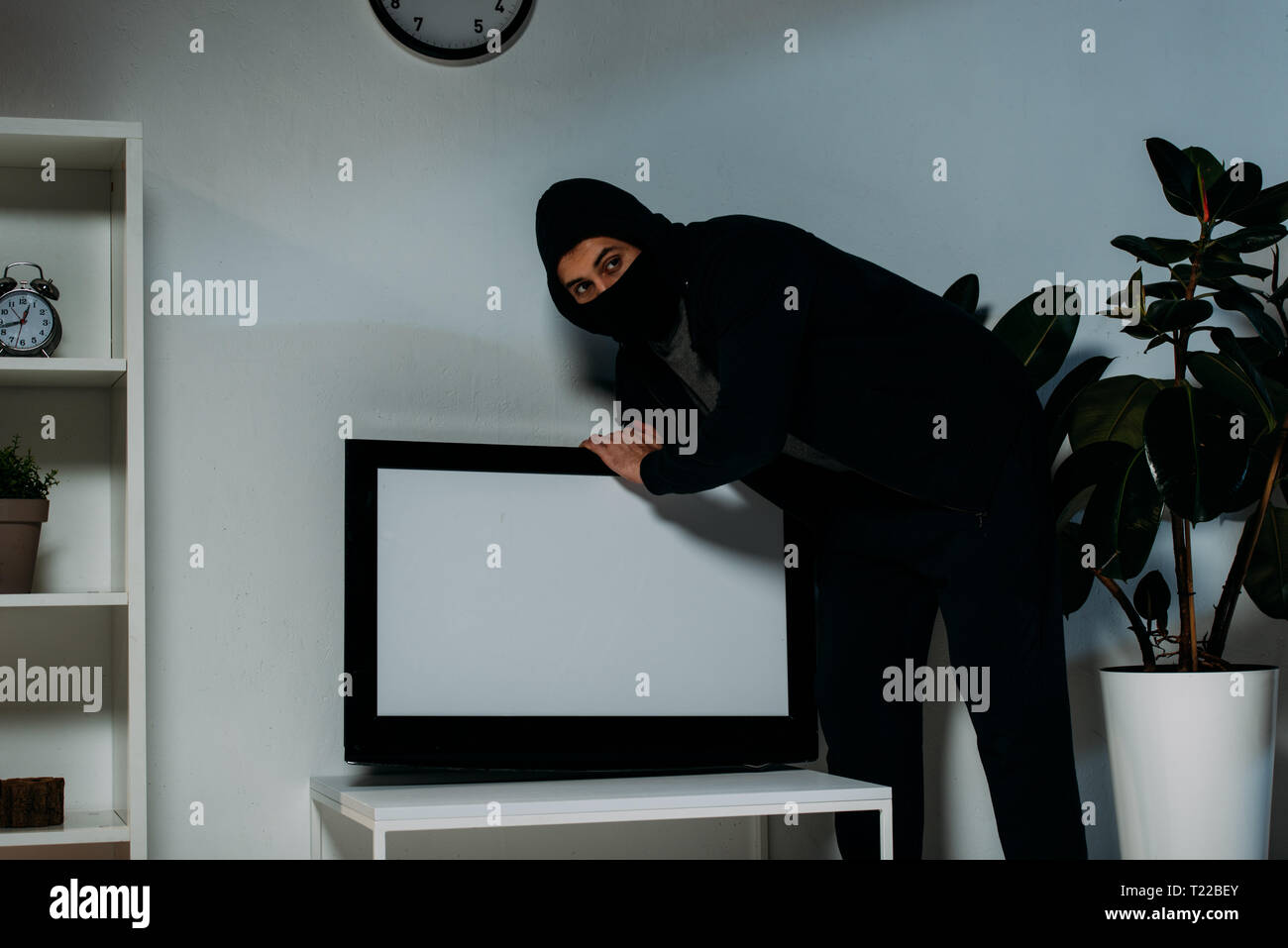 Suspicious robber in mask stealing flat-screen tv with blank screen ...
