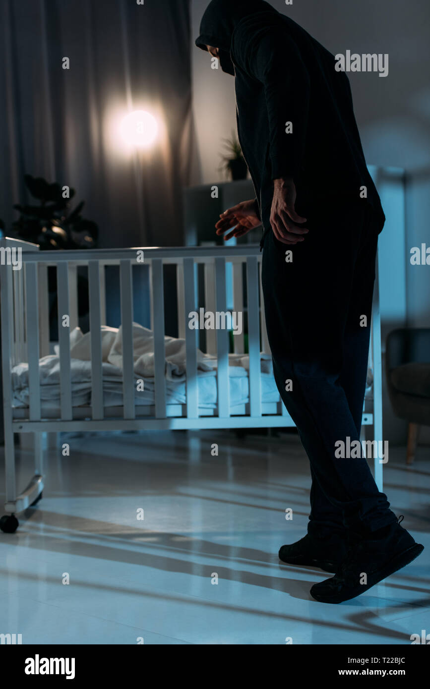 Kidnapper in black clothes standing near crib in dark room Stock Photo ...