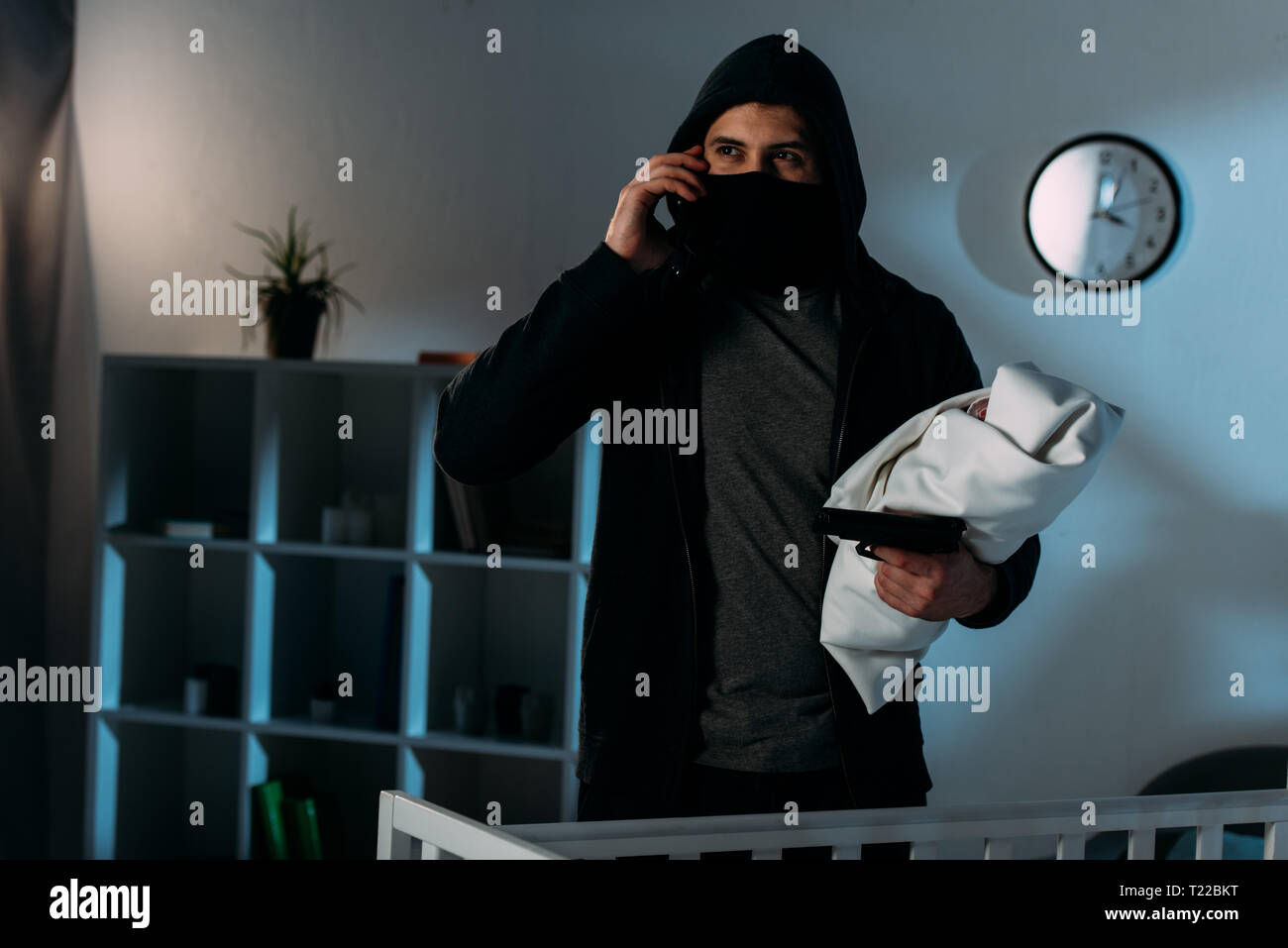 Kidnapper in mask with gun holding child and talking on smartphone ...