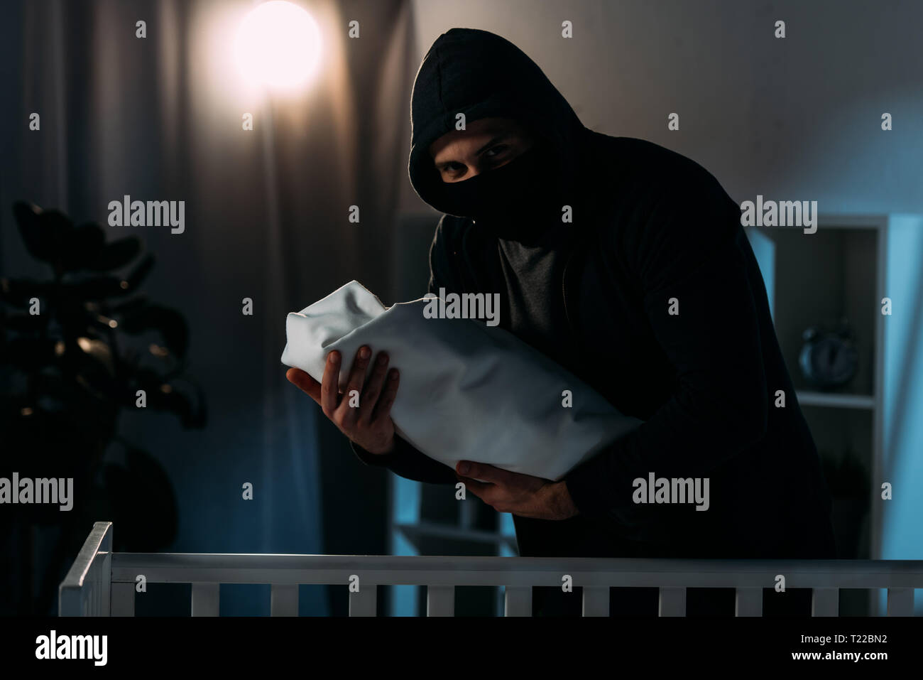 Kidnapper in mask and hoodie holding infant child in dark room Stock ...