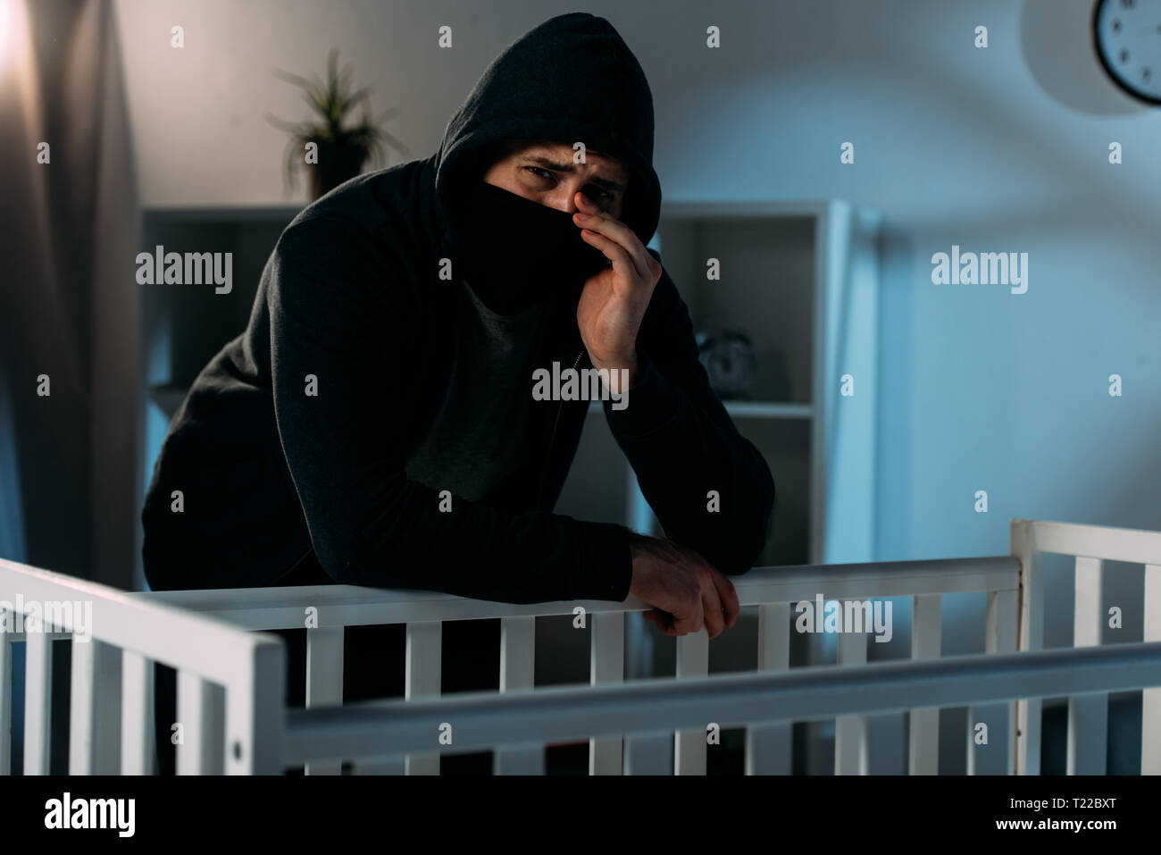 Crying kidnapper in mask standing near crib in dark room Stock Photo ...