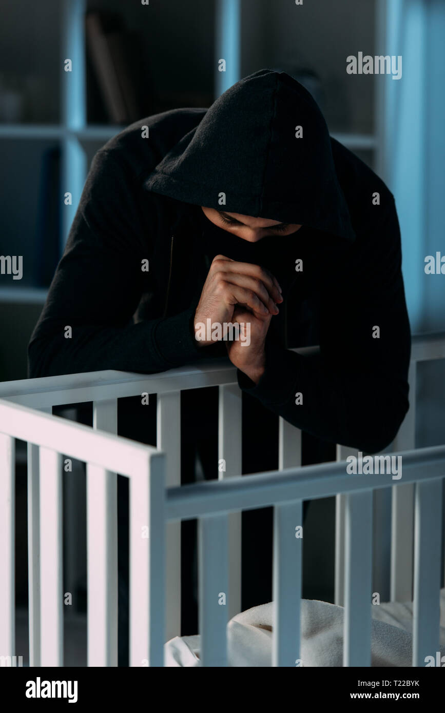 Kidnapper in black hoodie looking in crib and showing please gesture ...