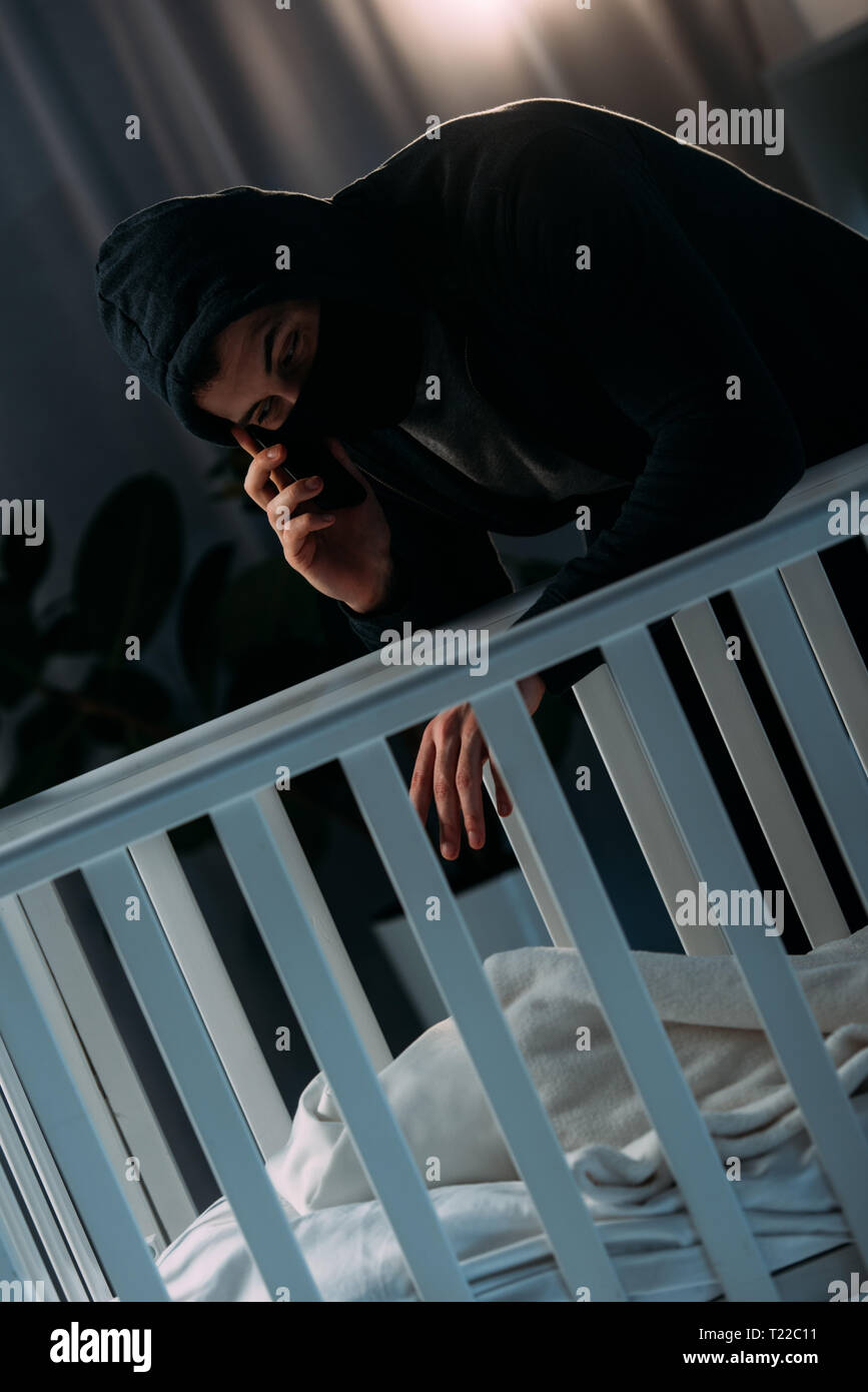 Kidnapper in mask talking on smartphone while standing near crib Stock ...