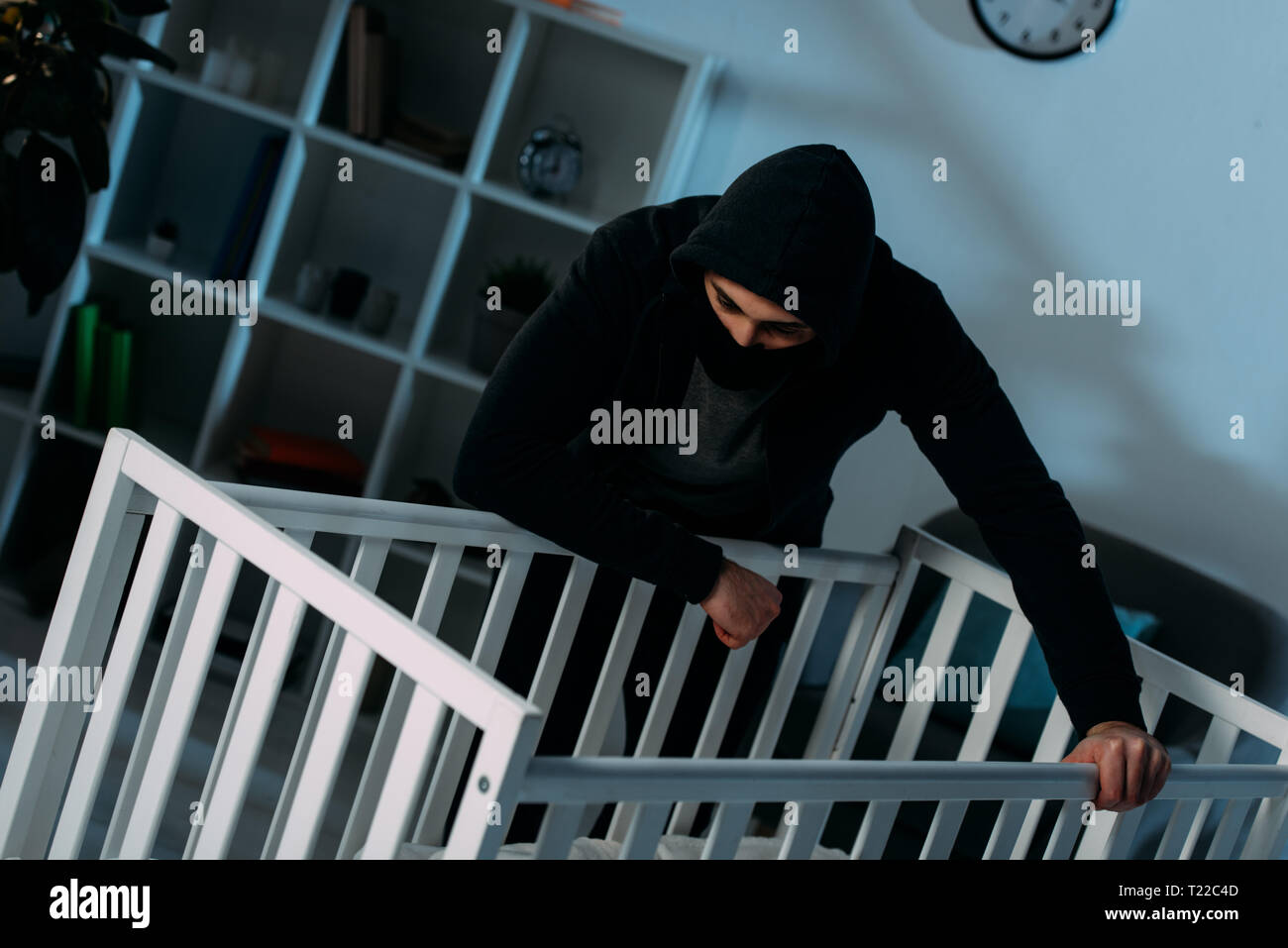 Kidnapper in black clothes standing in dark room and looking in crib ...