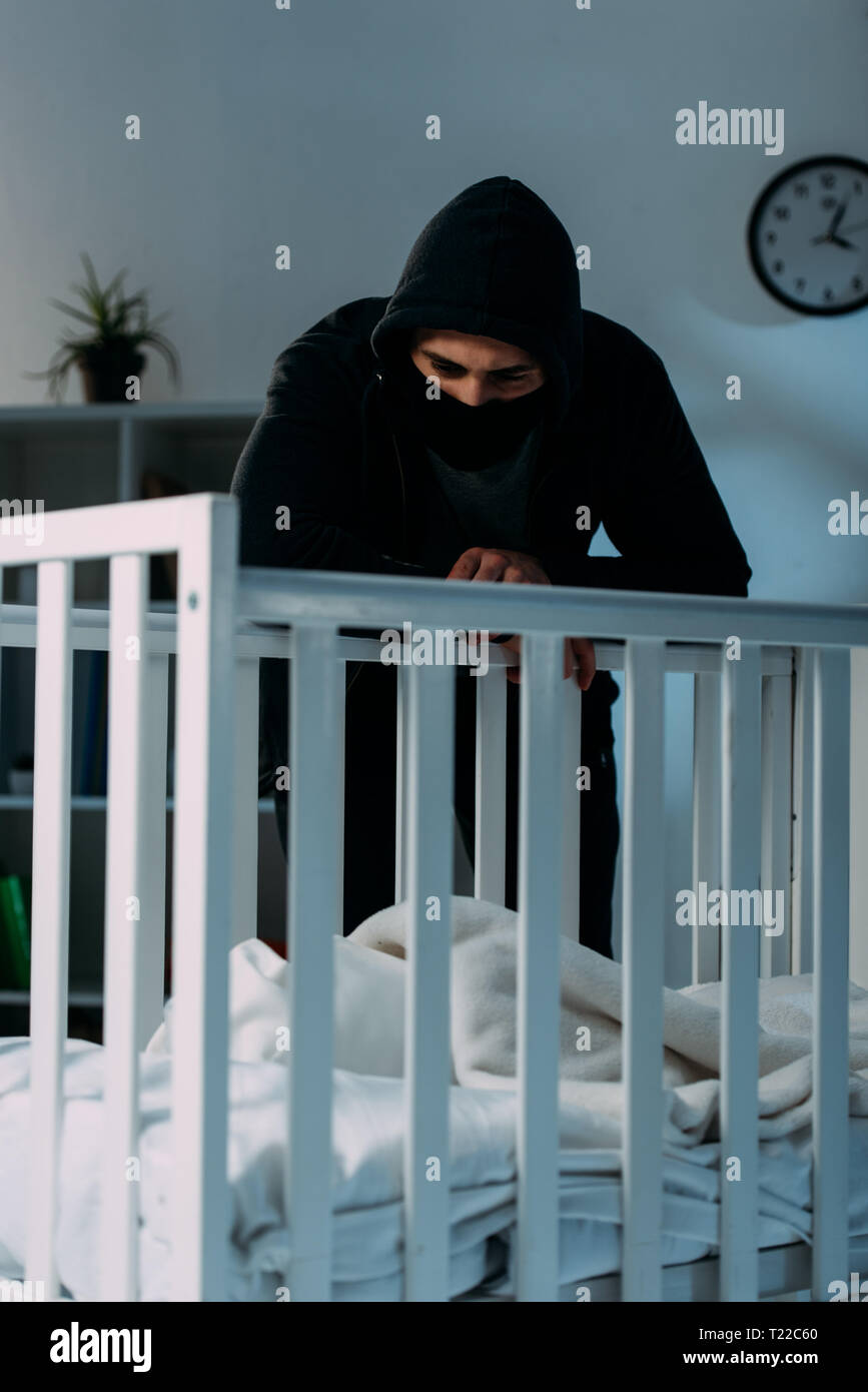 Pensive kidnapper standing in dark room and looking in crib Stock Photo ...