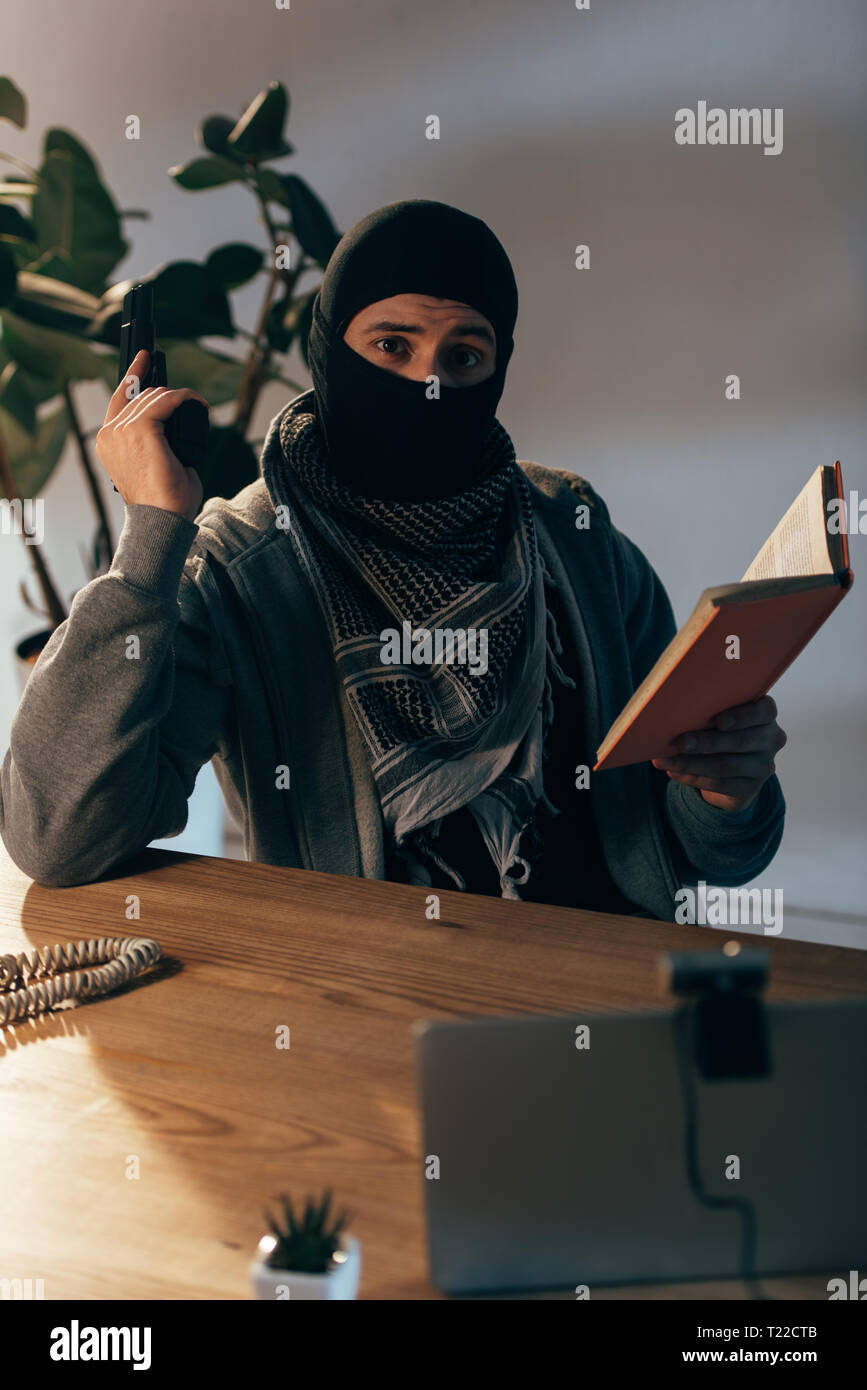 Terrorist in black mask holding gun and reading book Stock Photo - Alamy