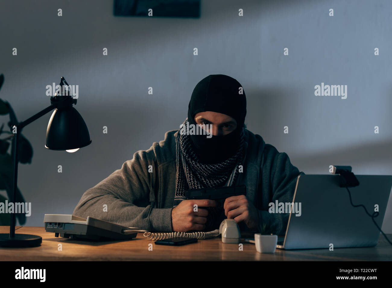 Aggressive terrorist sitting at table with gun and looking at camera ...