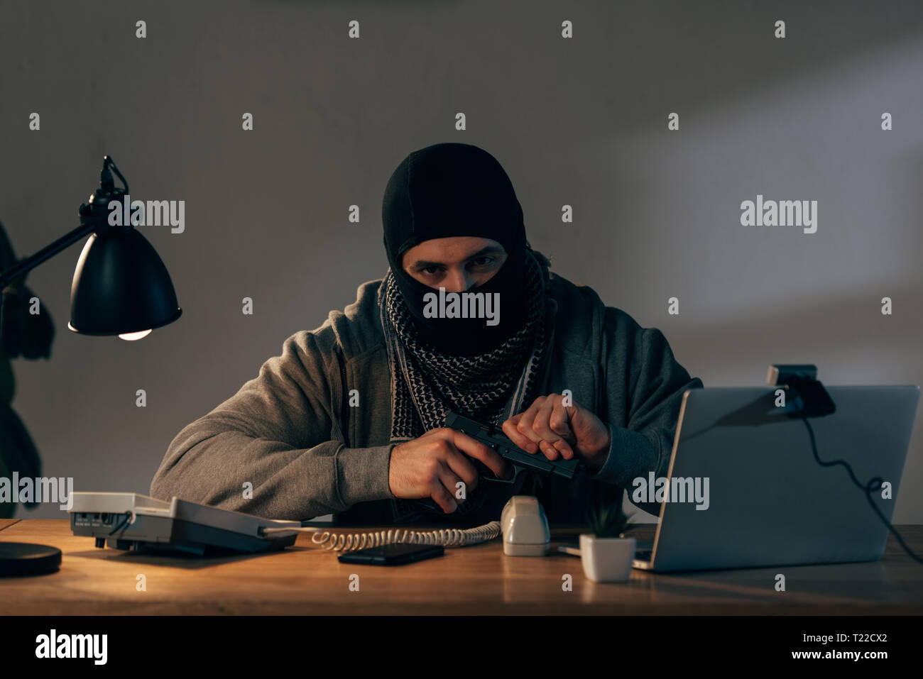 Terrorist in black mask sitting at table and loading gun Stock Photo ...