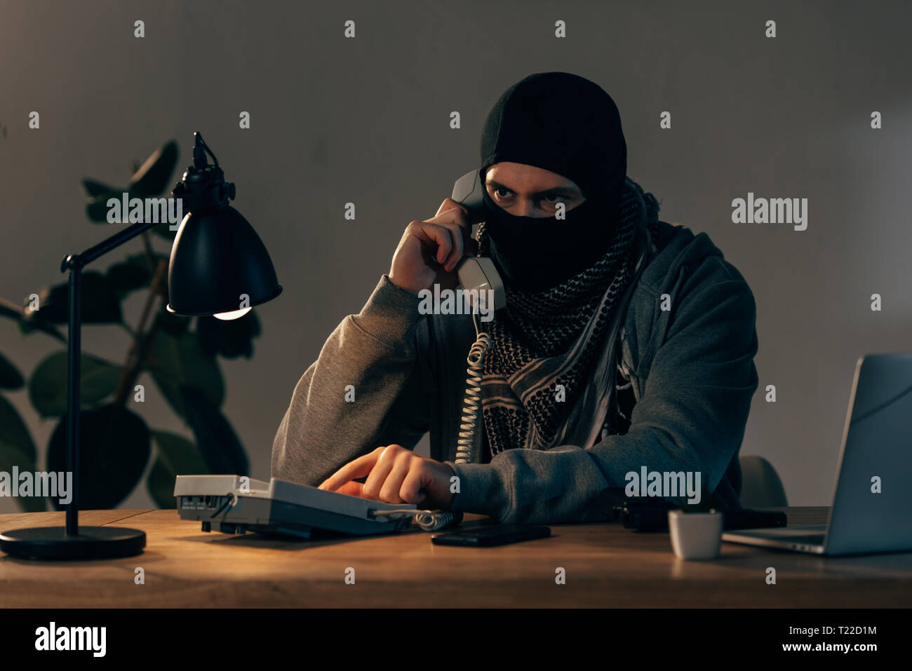 Serious criminal in black mask talking on telephone in room Stock Photo ...