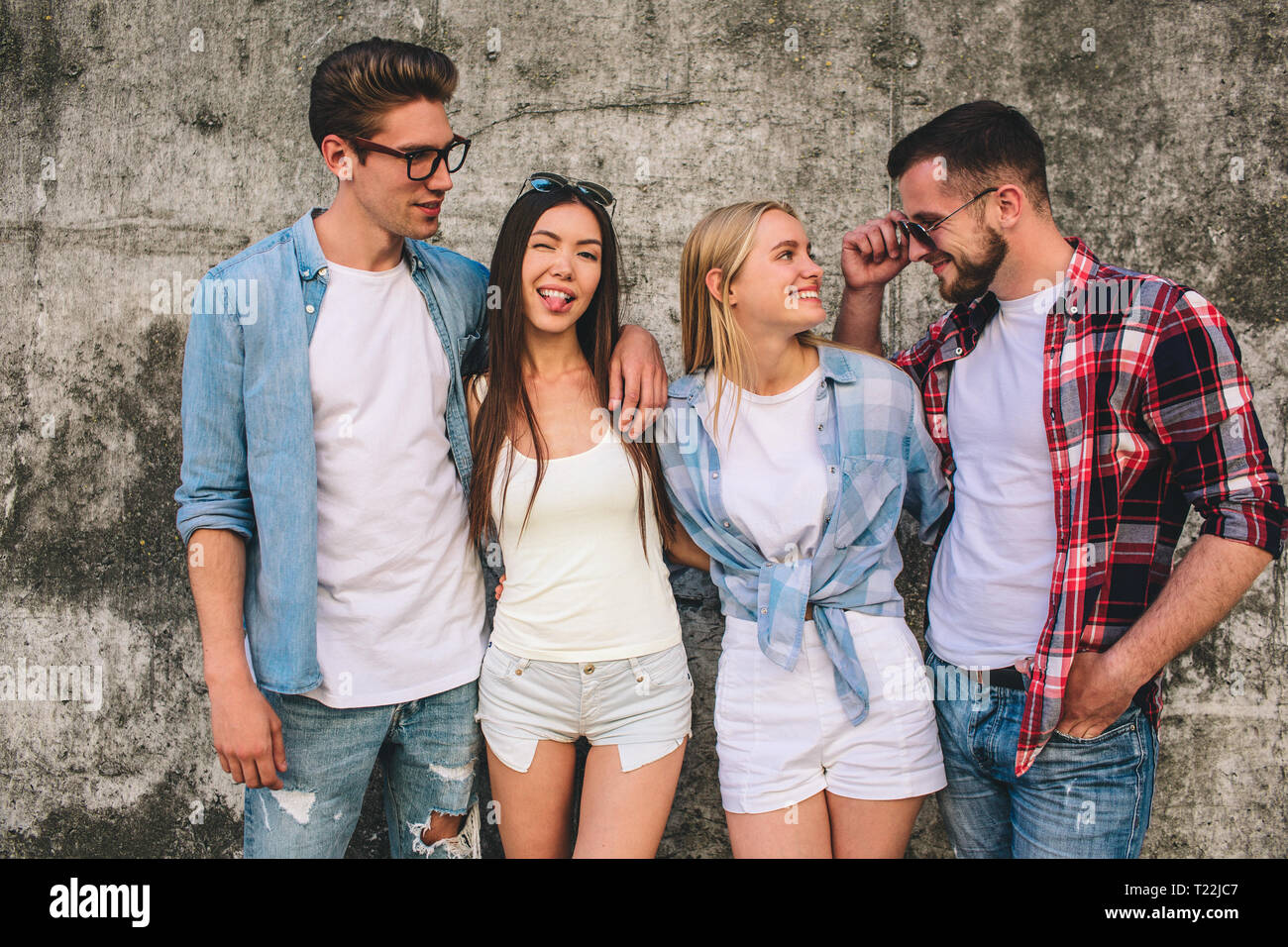 Two girls and two boys are standing together on grey background. Blonde ...