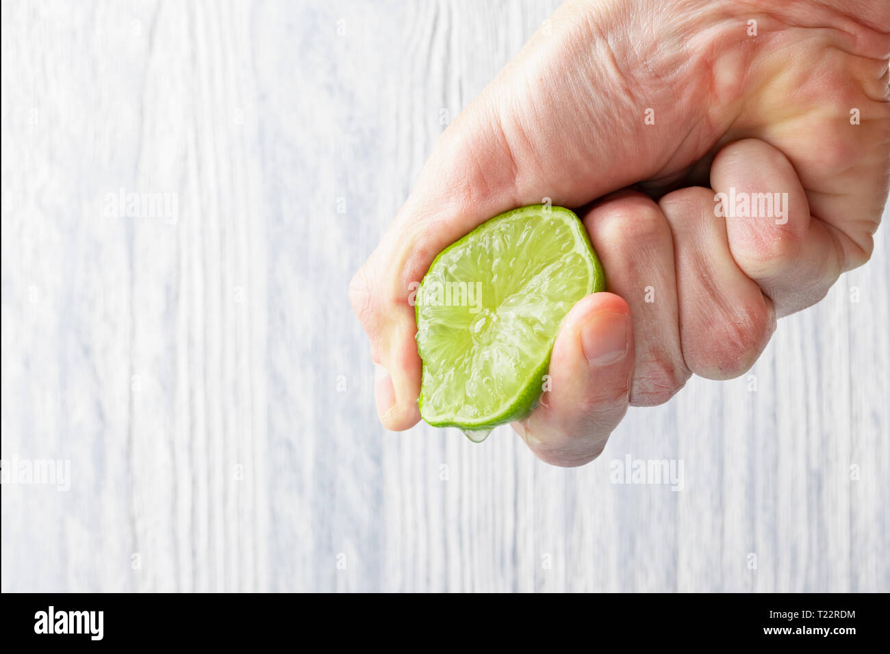 The hand of a man squeezes the juice from a slice of lime half. Juicy drop hanging down. Light ...