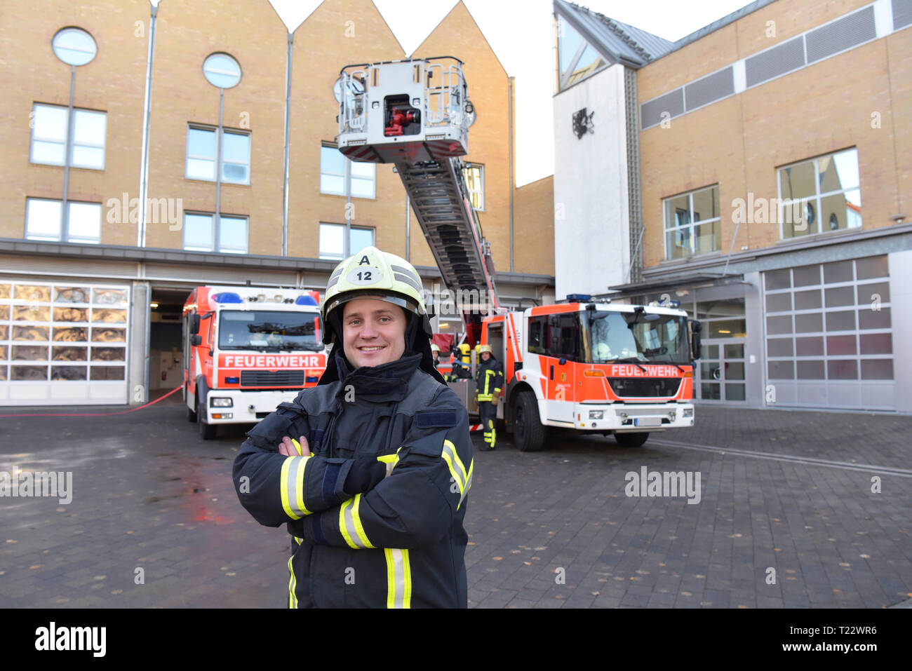 Portrait of smiling firefighter in front of fire engine with colleagues ...
