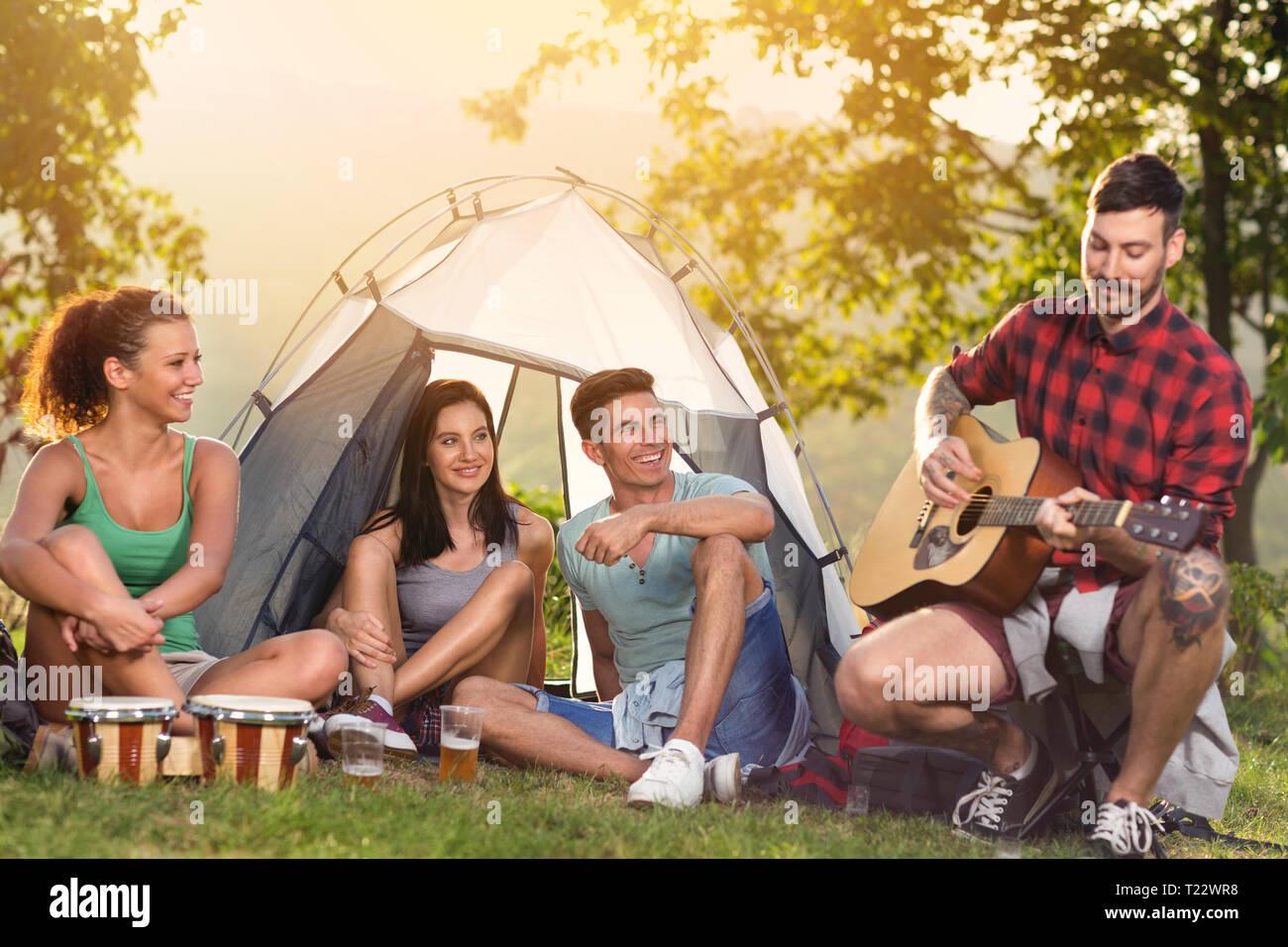 Young people enjoying in music on camping trip, sitting next tent and ...