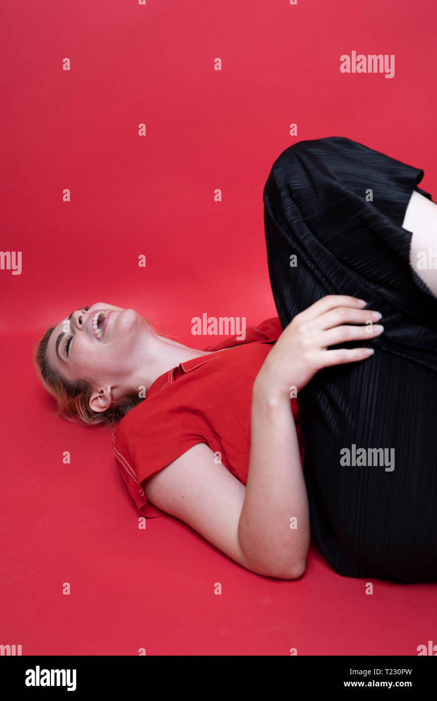 Laughing young woman lying on red background Stock Photo - Alamy