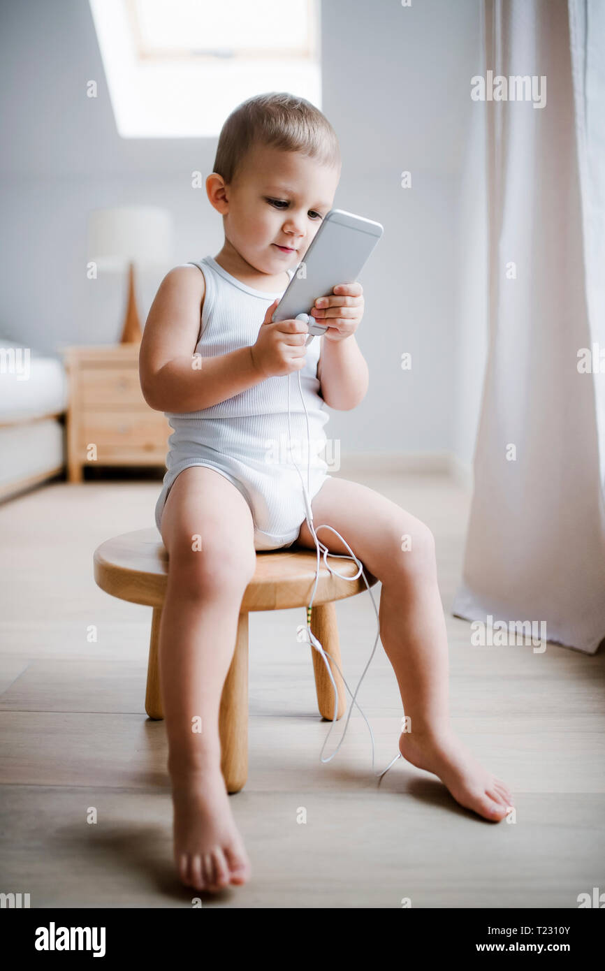 Toddler boy sitting on stool at home using smartphone Stock Photo - Alamy