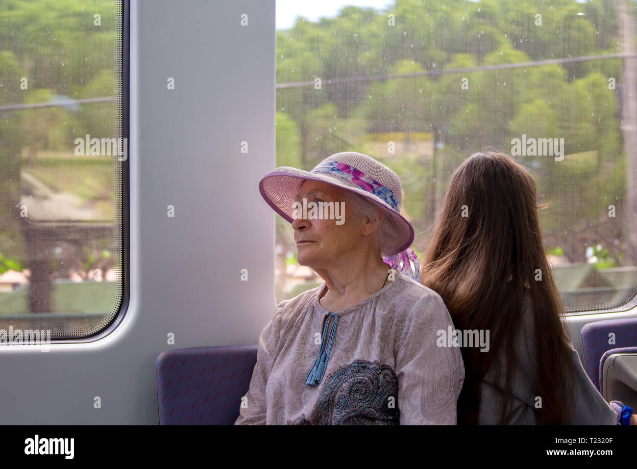 Beautiful gray-haired grandmother in a sunhat rides a commuter train ...