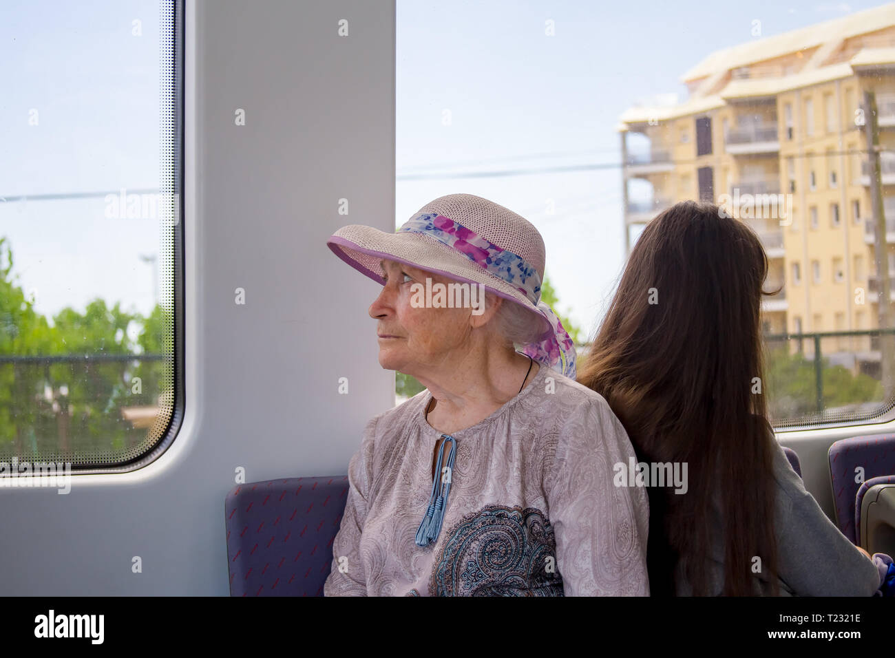Beautiful gray-haired grandmother in a sunhat rides a commuter train ...