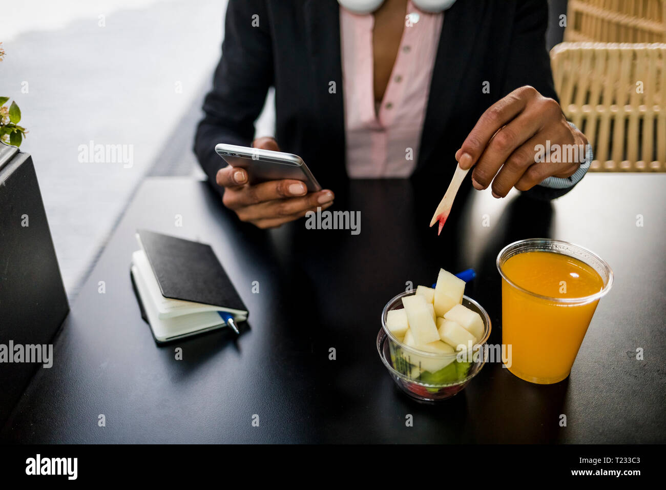 Businesswoman using cell phone at pavement cafe while eating fruit ...