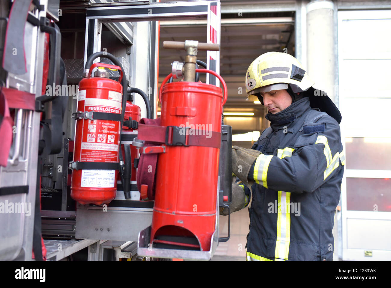 Firefighter standing at fire engine with fire extinguisher Stock Photo ...