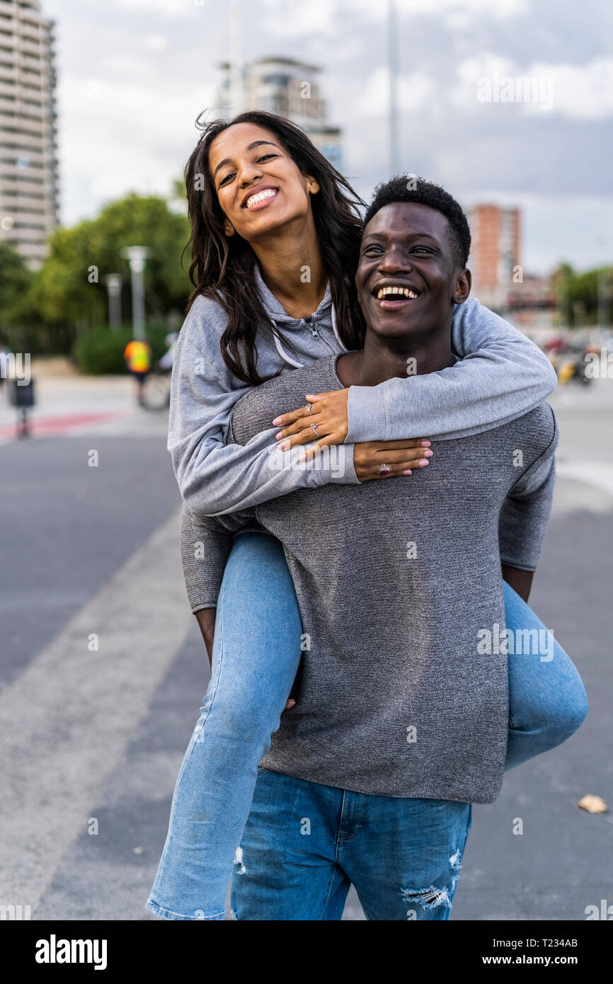 Young man carrying his girlfriend piggyback in the street Stock Photo ...