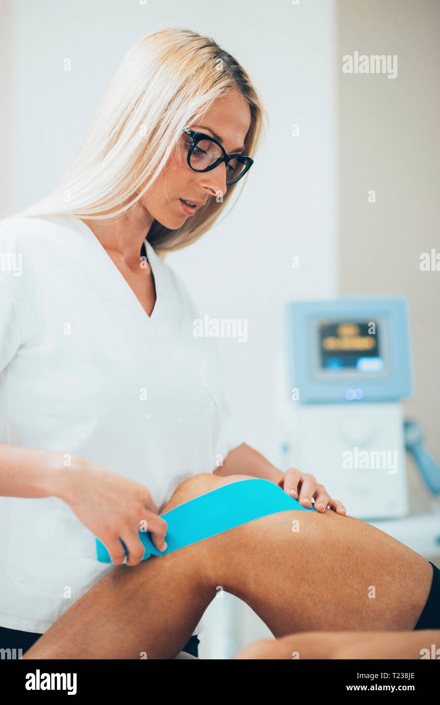 Kinesio taping in physical therapy. Therapist placing kinesio tape to patient's knee Stock Photo ...