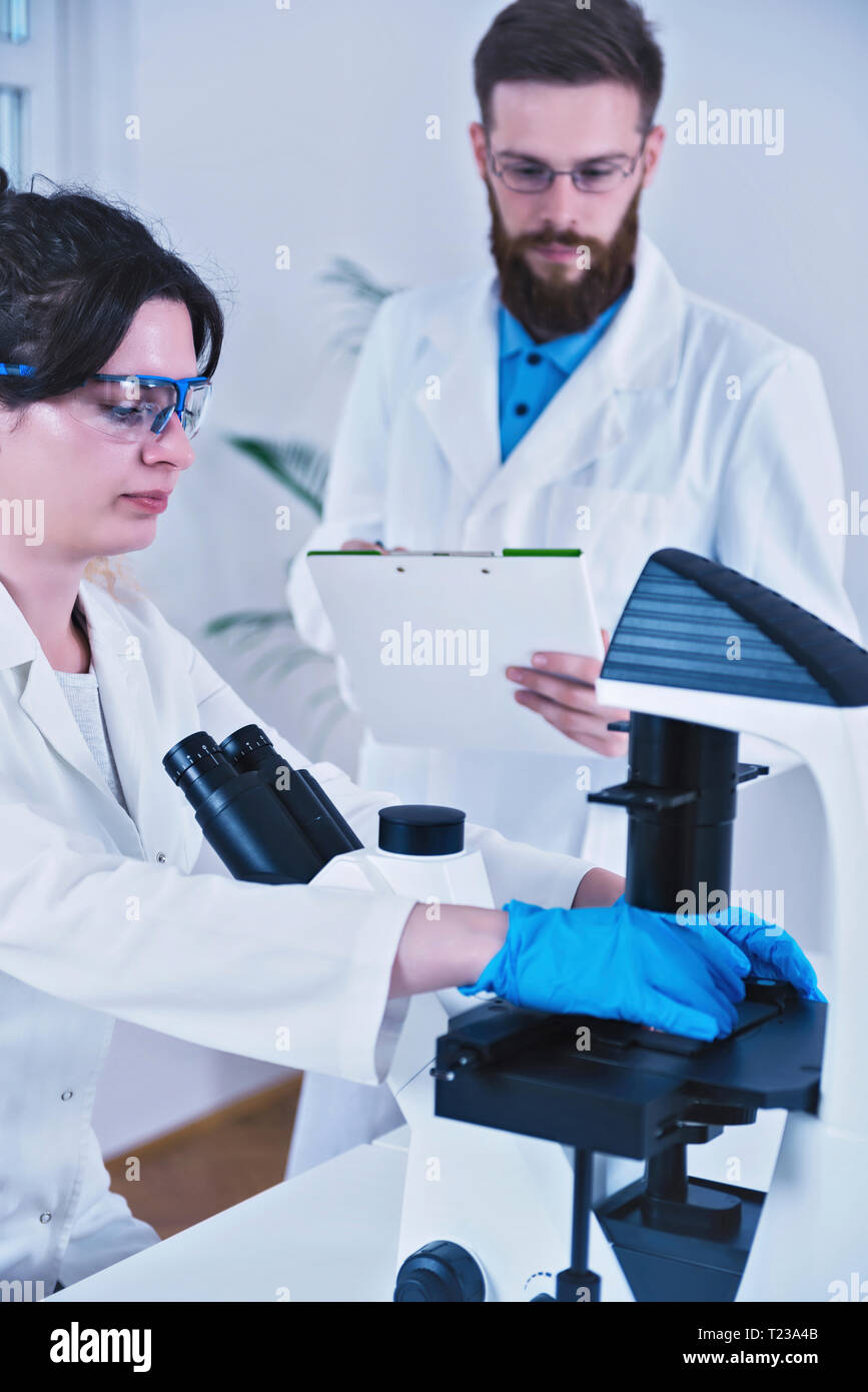 Young woman scientist doing test in laboratory with microscope, male ...
