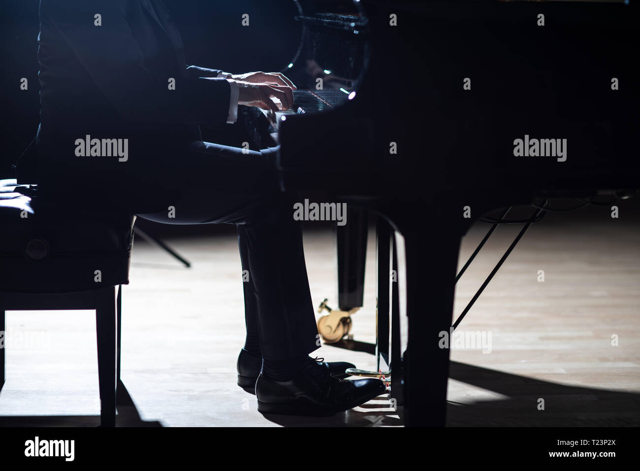 An elegant man in a black suit playing grand piano on stage in a ...