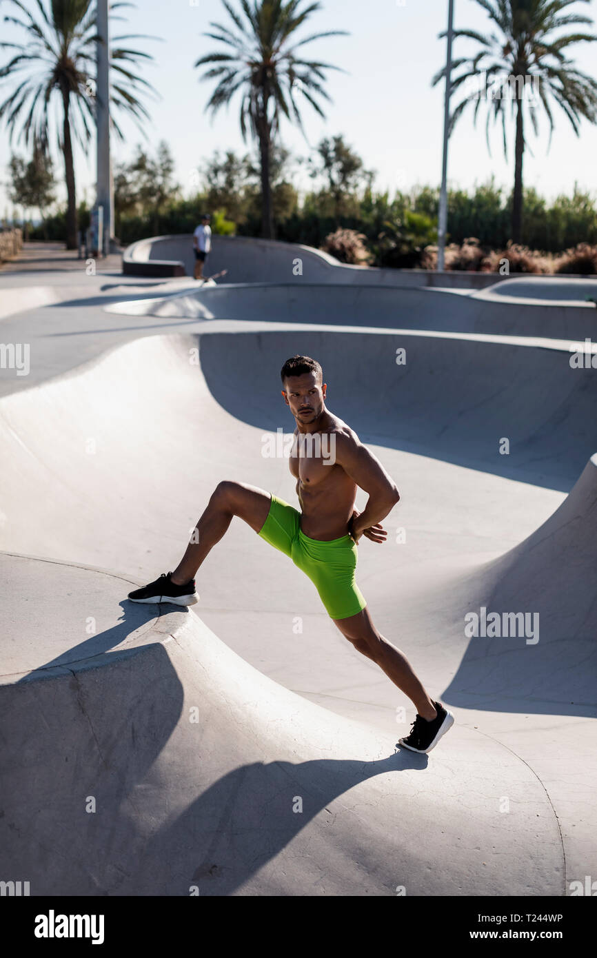 Barechested muscular man doing stretching exercise in a skatepark Stock ...