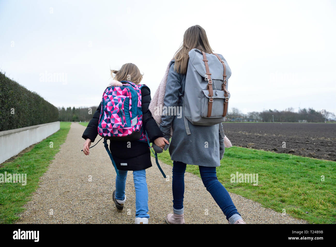 Back view of two sisters with backpacks walking hand in hand Stock ...