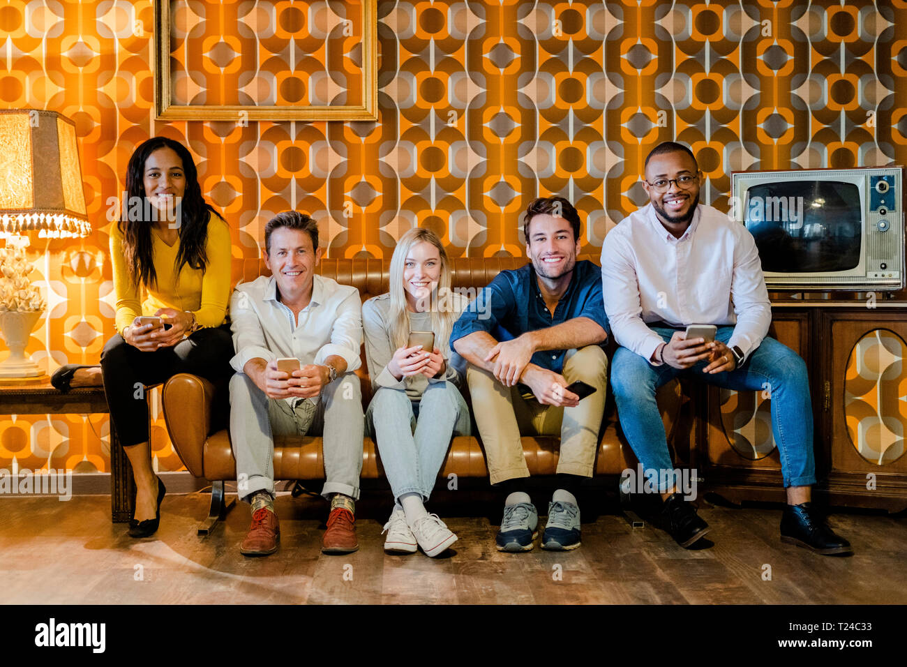 Group of smiling people sitting on couch in vintage living room holding ...
