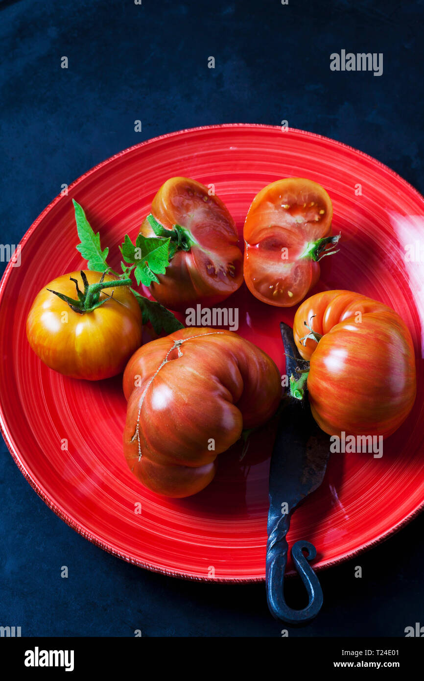 Whole and sliced beef tomatoes 'Chocolate Stripes' on red plate Stock ...