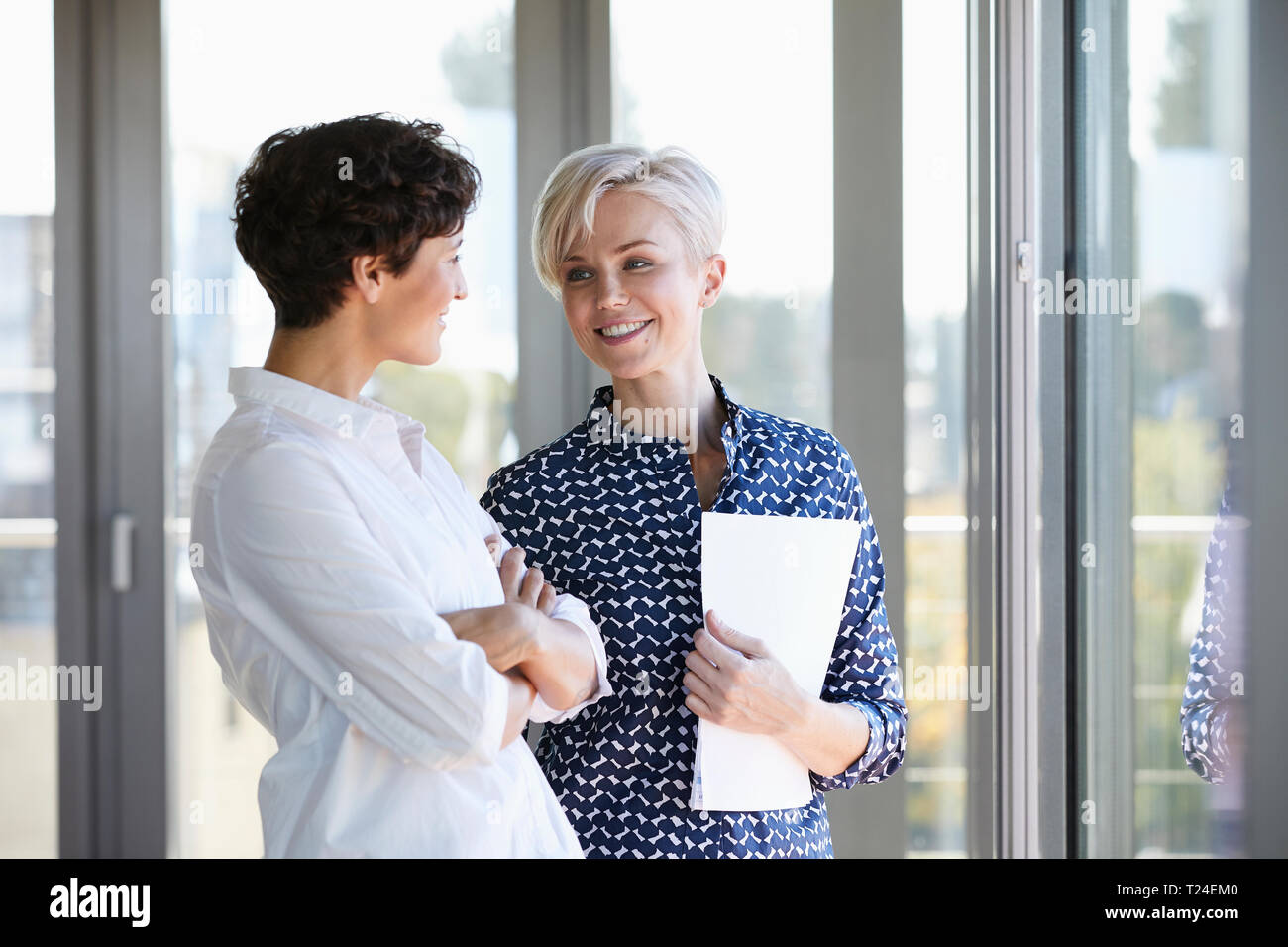 Two smiling businesswomen talking at the window in office Stock Photo ...
