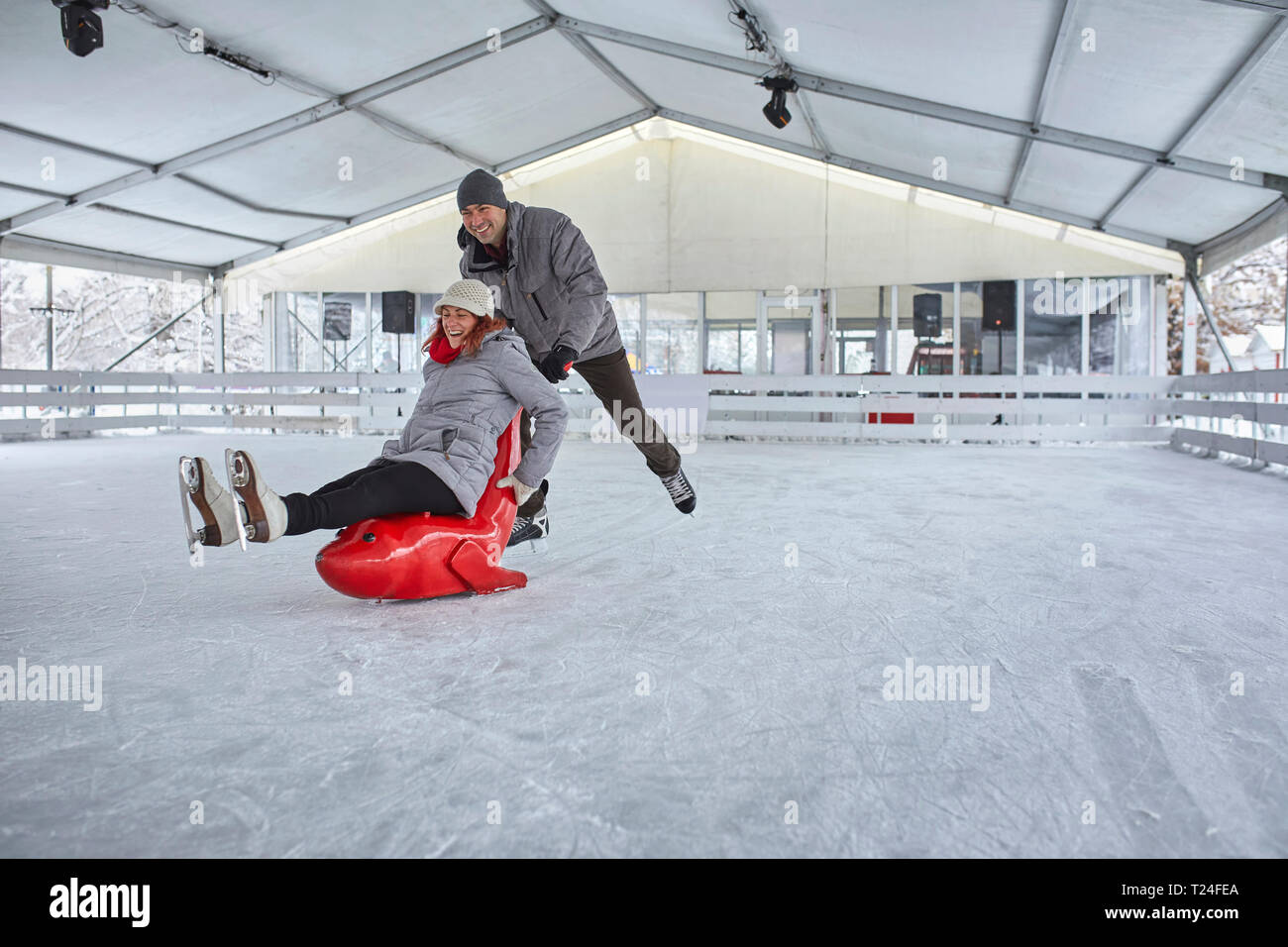 Couple ice skating, using seal sledge to push woman Stock Photo - Alamy