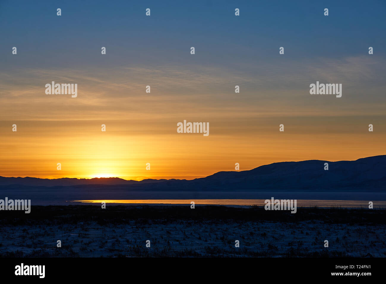 The sun sets over Utah Lake on a clear winter evening, with snow on the ...
