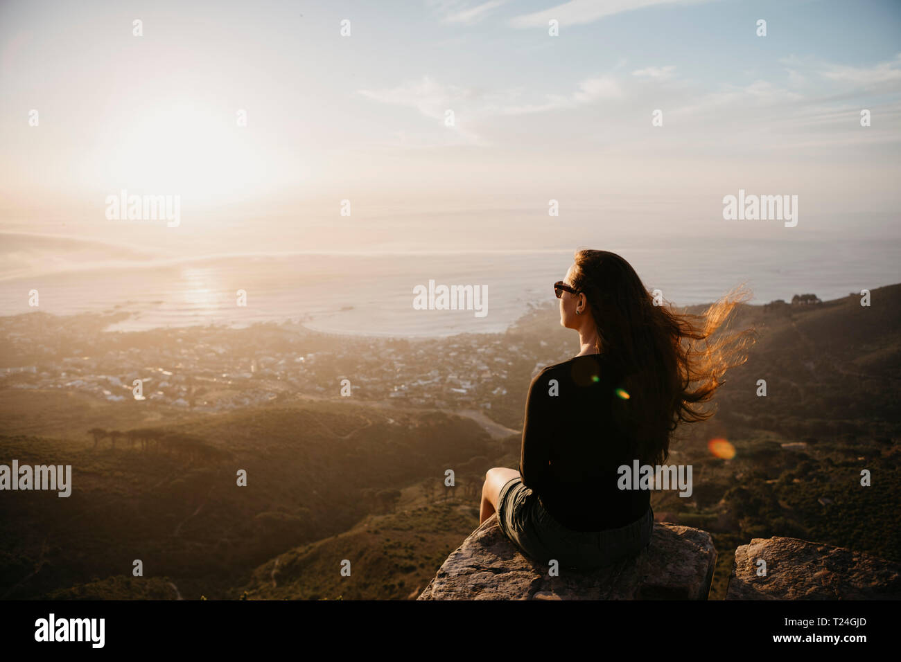 South Africa, Cape Town, Kloof Nek, woman sitting on rock at sunset ...