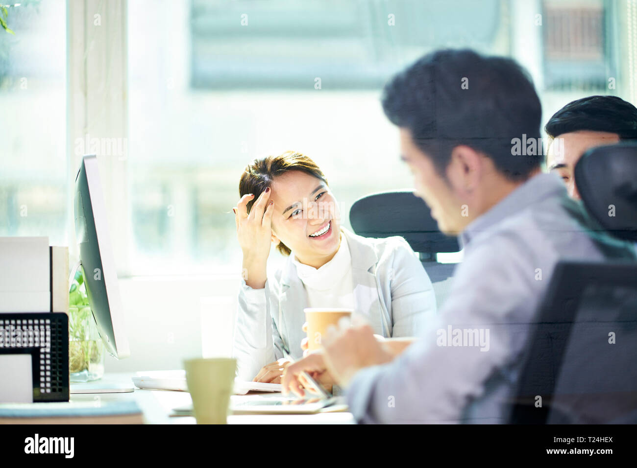 three young asian entrepreneurs sitting at desk discussing business ...