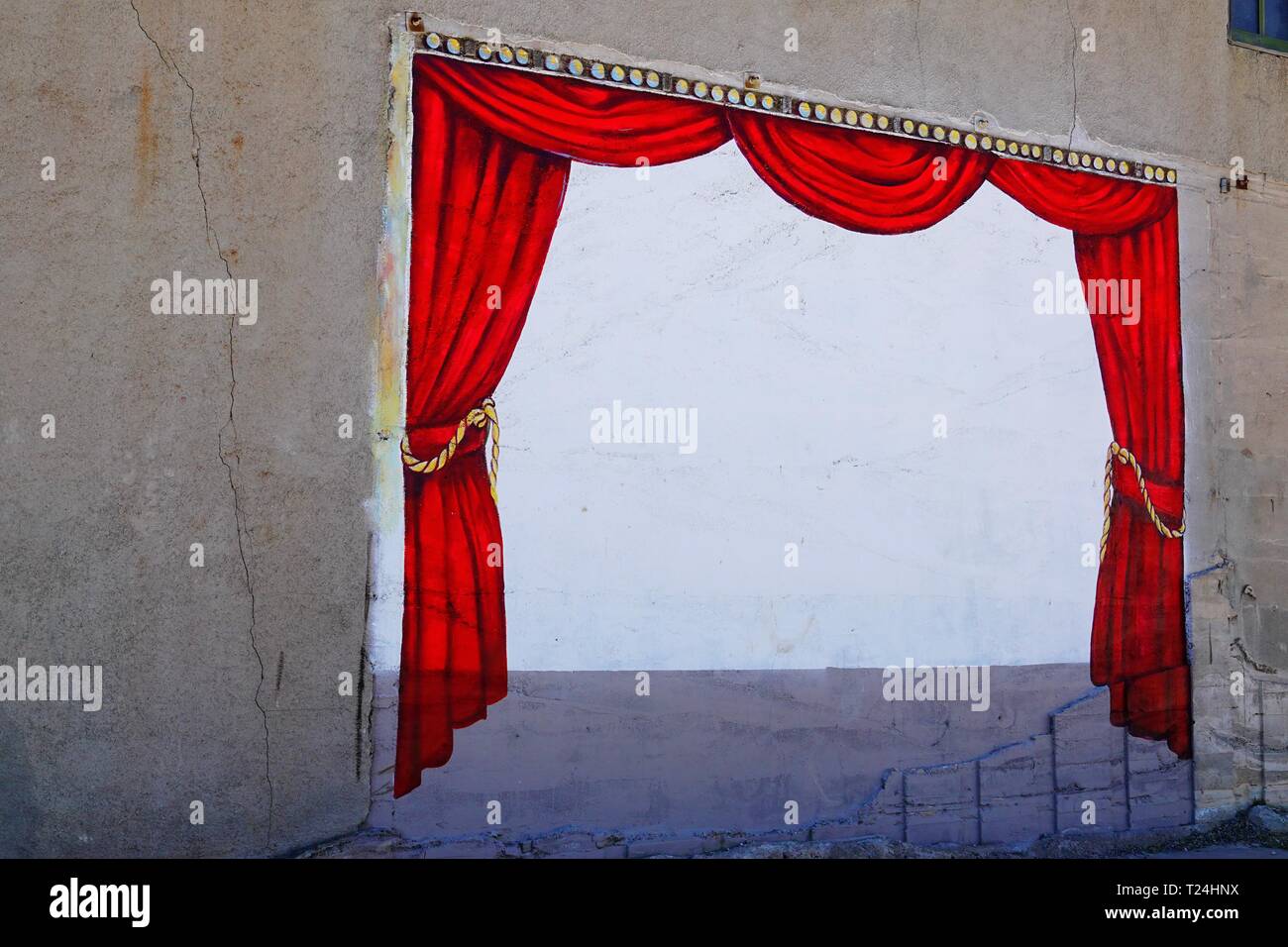 A mural of a stage with a red curtain is painted on the side of a wall ...