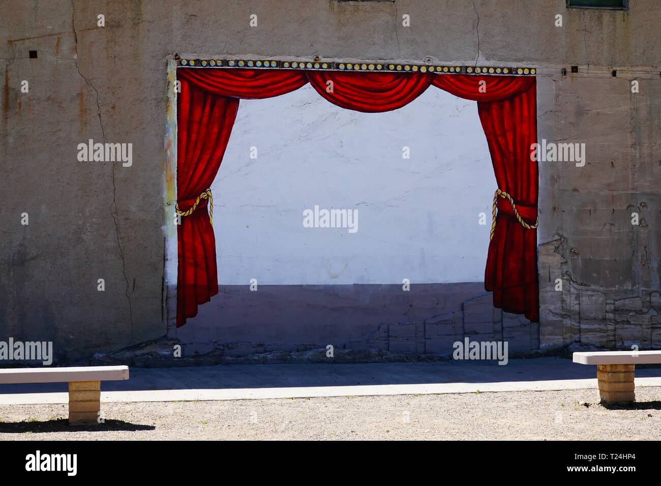 A mural of a stage with a red curtain is painted on the side of a wall ...