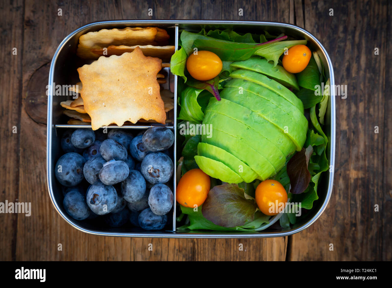 Lunch box of leaf salad, avocado, blueberries, tomatoes and crackers ...