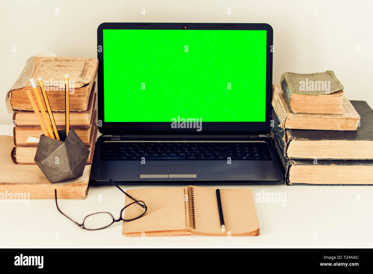 Green screen laptop, stack of old books, notebook and pencils on white ...