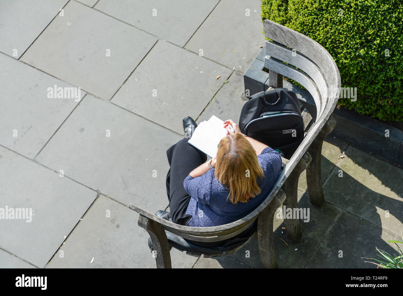 A single woman on a park bench writing on a notepad Stock Photo - Alamy