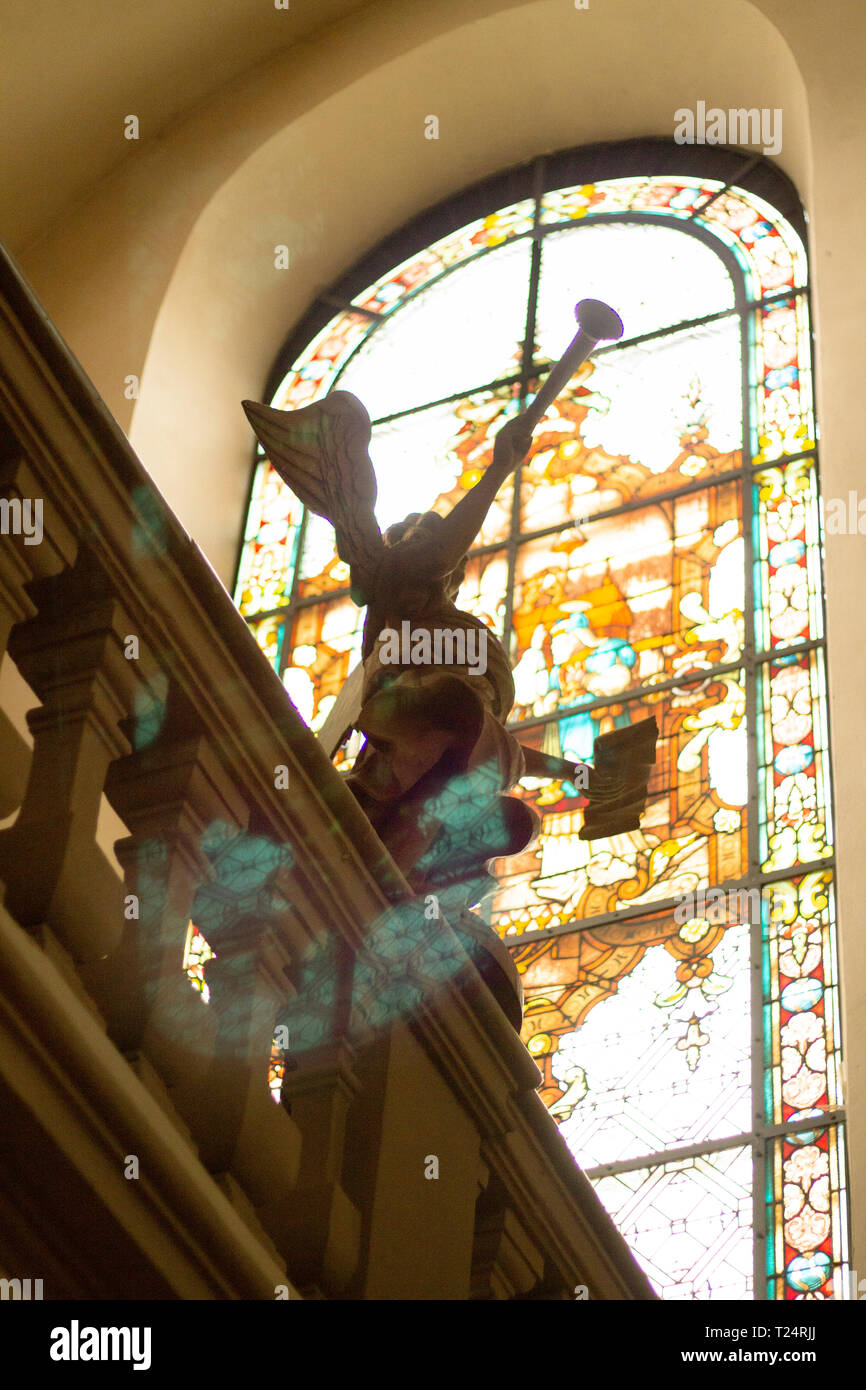 The sun shines through a stained glass window onto an angel in a church ...