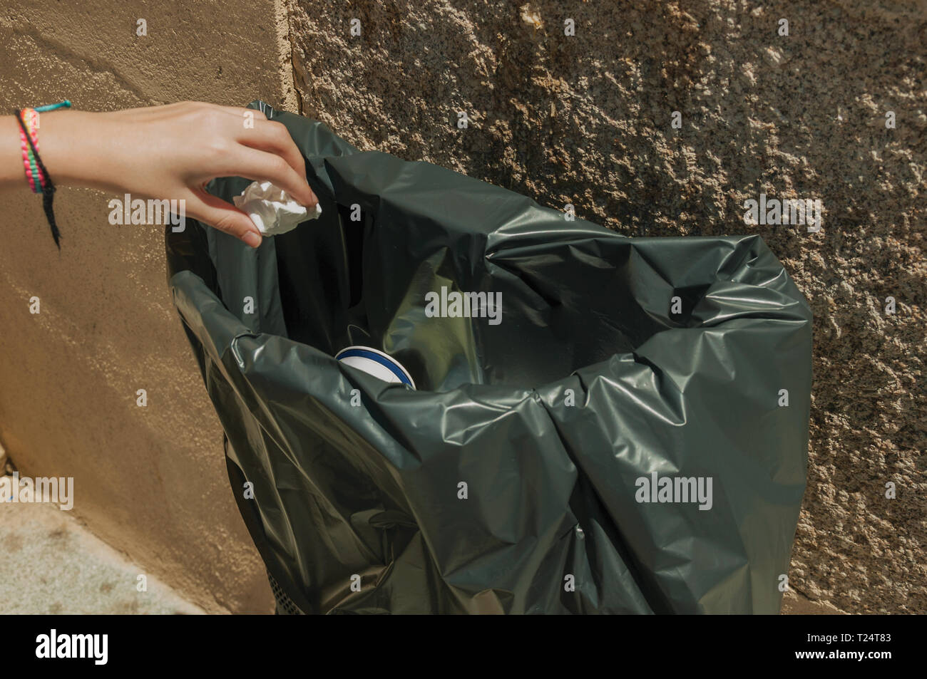 Hand of girl throwing waste in a trash can next to a wall, in a sunny ...